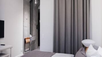 Quarto de hotel moderno com uma cama grande, uma mesinha de cabeceira, uma escrivaninha e um banheiro visível por uma porta aberta.