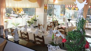 Uma sala de jantar com mesas postas para refeição, cadeiras e diversos objetos decorativos, incluindo flores e uma escultura de pássaro.