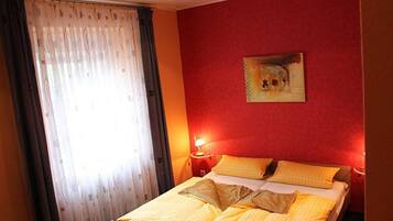 Um quarto com uma cama, um quadro na parede e uma janela com cortinas.