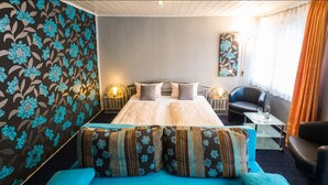 Quarto de hotel com cama, sofá, poltrona e pequena mesa com abajur.