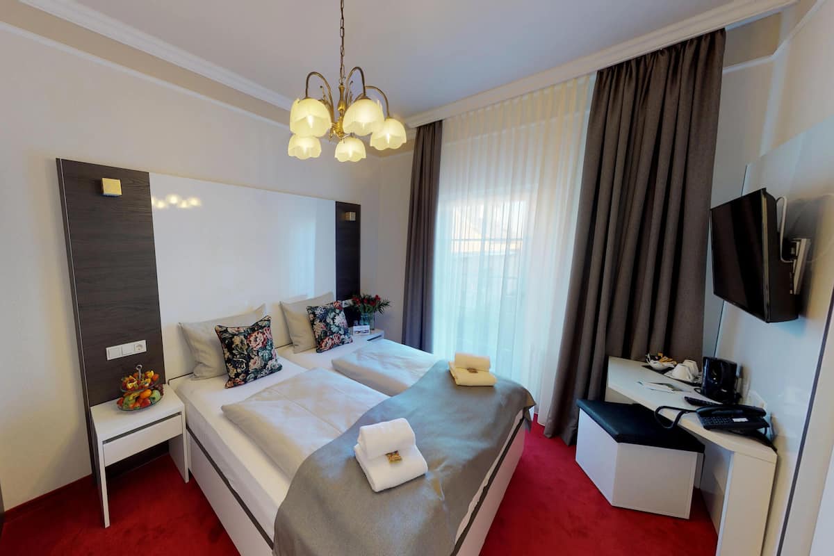 Quarto de hotel com uma cama grande, uma escrivaninha com computador, televisão e um tapete vermelho.