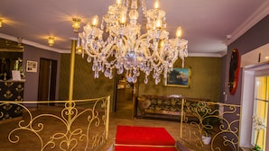 Um hall imponente com um grande lustre de cristal, escadas com carpete vermelho e grades douradas ricamente decoradas.