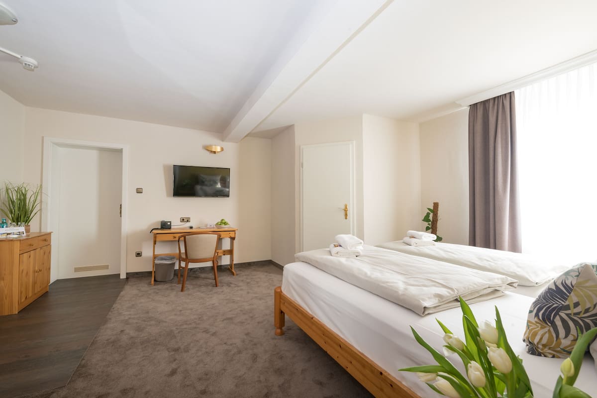 Quarto de hotel com cama, escrivaninha, cadeira, televisão e janela com cortinas.