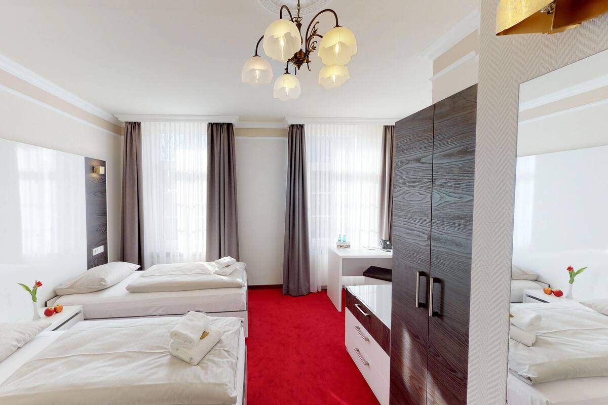 Quarto de hotel com duas camas, uma escrivaninha, um guarda-roupa e um candelabro.