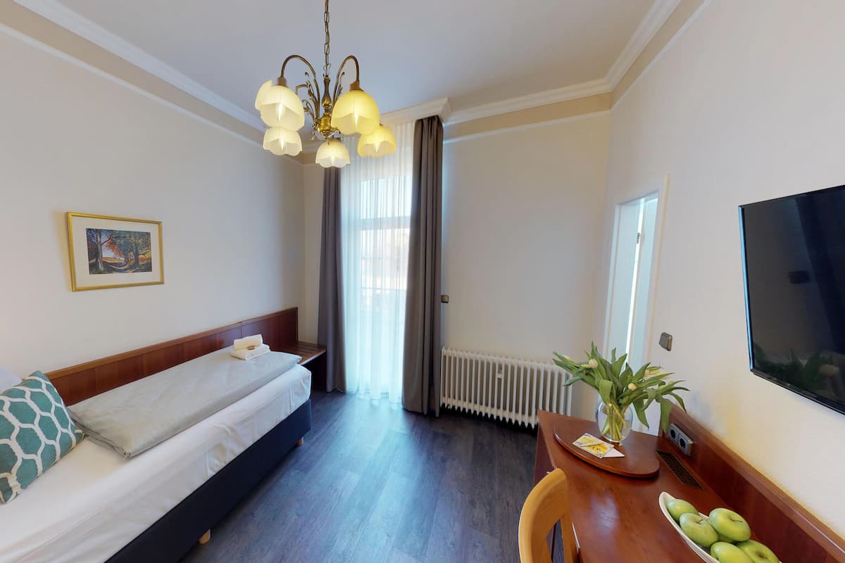 Quarto de hotel com cama, escrivaninha com planta, televisão e radiador.
