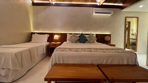 Quarto com duas camas de solteiro, um banco de madeira, mesa de cabeceira com abajur e teto com vigas de madeira e iluminação embutida.