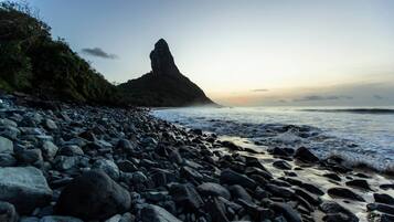 Uma praia rochosa com uma formação rochosa imponente ao longe.