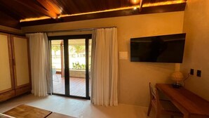 Quarto com cama, escrivaninha, televisão e porta de correr de vidro que dá para área externa.