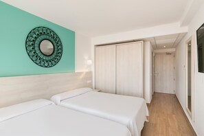 Quarto de hotel com duas camas, uma parede de destaque azul-turquesa, um espelho decorativo e um guarda-roupa.