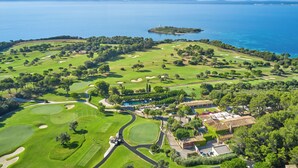 Um campo de golfe com piscina, rodeado por vegetação exuberante e vista para o mar.