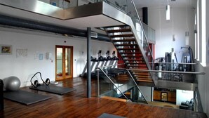 Uma academia com vários níveis, uma escada, equipamentos de ginástica e piso de madeira.