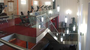 Academia moderna com equipamentos de ginástica, escadas e guarda-corpo de vidro.