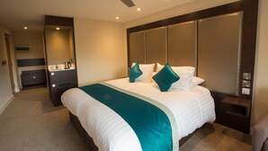 Quarto de hotel com uma cama grande, um ventilador de teto, uma mesa de cabeceira e um criado-mudo.