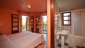 Quarto com cama, banheiro com pia e espelho, e vista pela janela com cortinas.