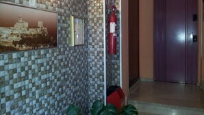 Um corredor com paredes de piso xadrez, um extintor preso na parede, uma porta e uma pequena planta.