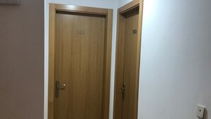 Um corredor com duas portas de madeira, cada uma marcada com um número. O chão é revestido com um padrão de mármore.