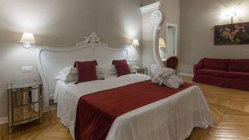 Quarto com cama grande, duas luminárias de cabeceira, espelho, sofá vermelho e piso de madeira.