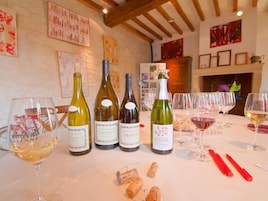 Disposição para degustação de vinhos com garrafas e copos sobre uma mesa, vigas de madeira no teto e obras de arte emolduradas nas paredes.