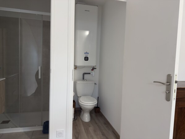 Casa de banho com sanita, cabine de duche e parede branca.