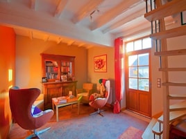 Quarto acolhedor com estante de madeira, poltrona vermelha, mesa pequena e janela com cortinas.