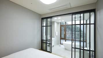 Quarto moderno com uma cama grande, porta de vidro deslizante que dá para uma varanda com banheira e vista para o verde lá fora.