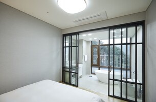 Quarto moderno com uma cama grande, porta de vidro deslizante que dá para uma varanda com banheira e vista para o verde lá fora.
