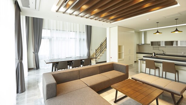 Uma sala de estar moderna com sofá, mesa de centro e área de jantar com mesa e cadeiras. Há também uma cozinha com bancada e cadeiras.