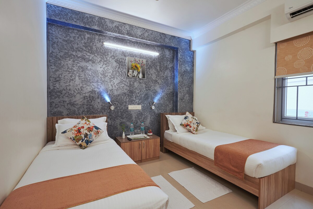 Quarto de hotel com duas camas, uma mesa de cabeceira, ar-condicionado na parede e janela com vista.
