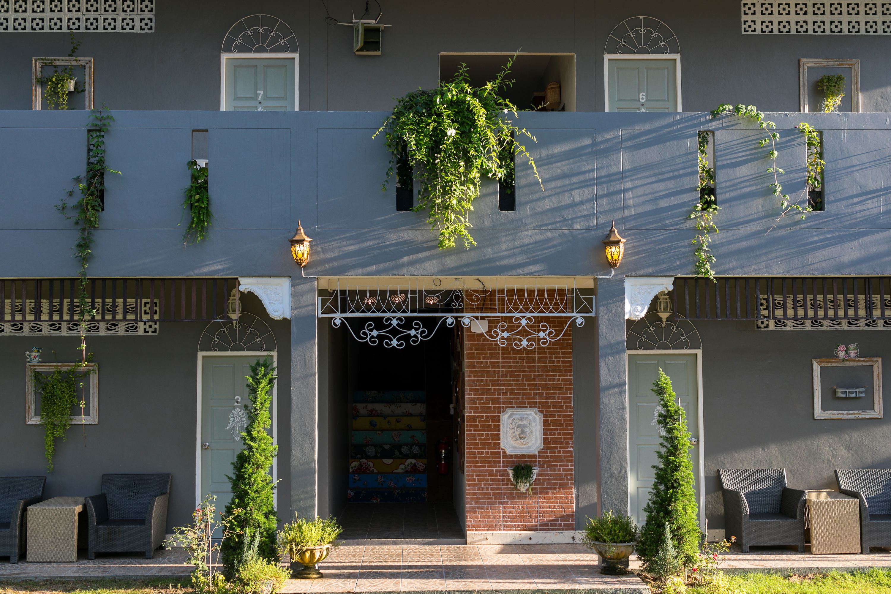 Entrada de hotel com fachada de tijolos, porta colorida e varanda com plantas penduradas.