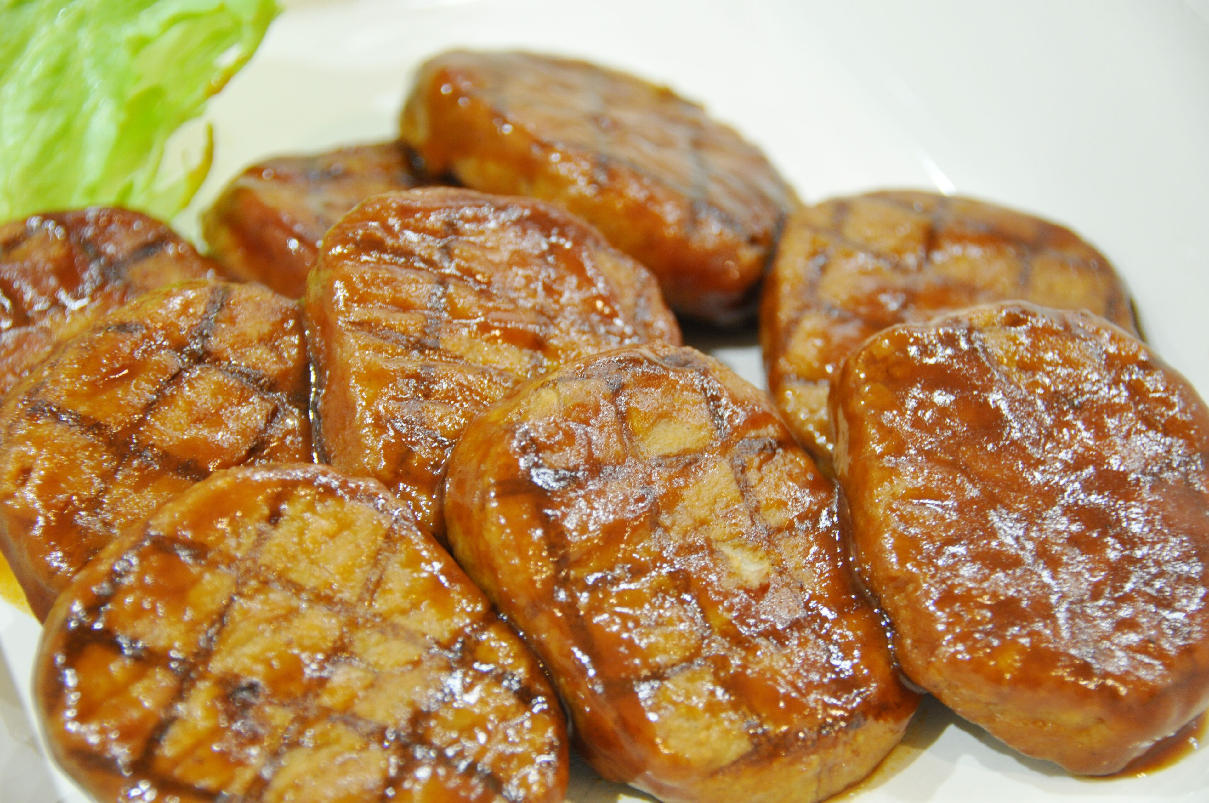 Um prato de carne grelhada com molho brilhante, acompanhado de alface verde.