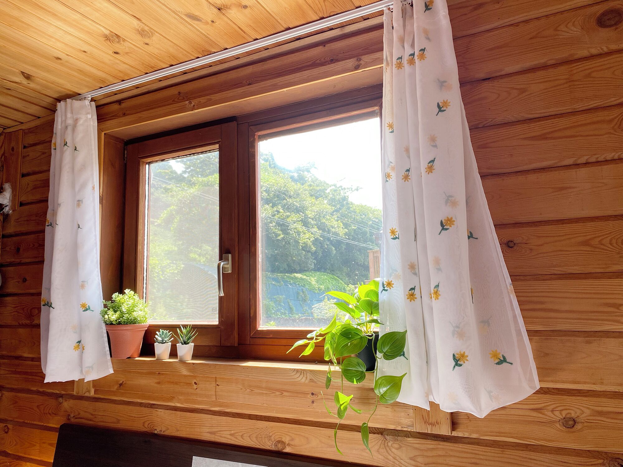 Um quarto de cabana de madeira com janela, cortinas e plantas em vasos.