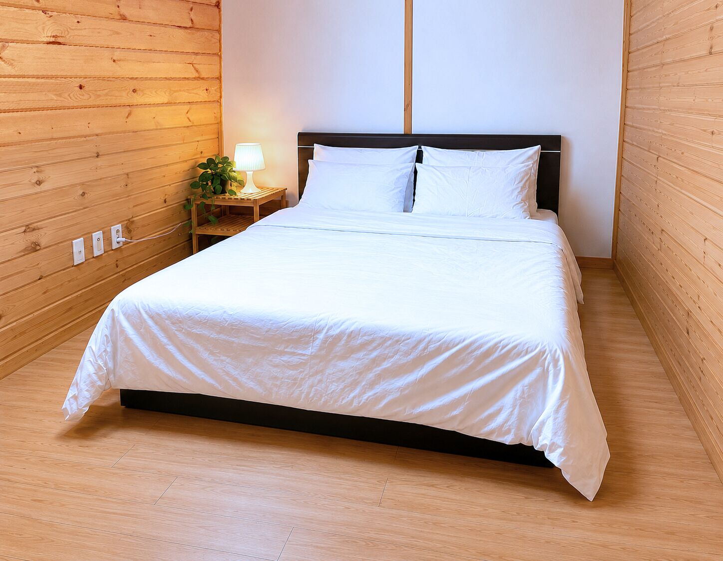 Cama bem arrumada em quarto com paredes de madeira e mesa de cabeceira com abajur.