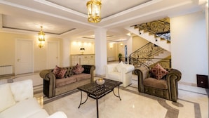 Uma sala de estar ampla, com teto alto, lustres elegantes e escadaria com grades ornamentadas.
