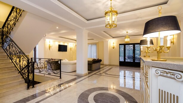 Um hall imponente com piso de mármore, escada com corrimão preto e lustres elegantes.