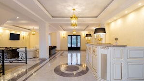 Um hall amplo com piso de mármore, um balcão de recepção e um grande lustre.
