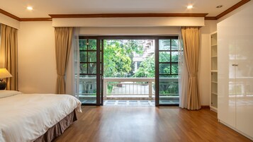 Quarto com uma grande porta de vidro deslizante que dá para uma varanda com vista para áreas verdes e edifícios.