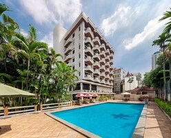 Um hotel com piscina, rodeado por palmeiras e um céu claro.