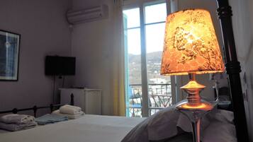 Quarto de hotel com cama, luminária, TV e janela com vista para o exterior.