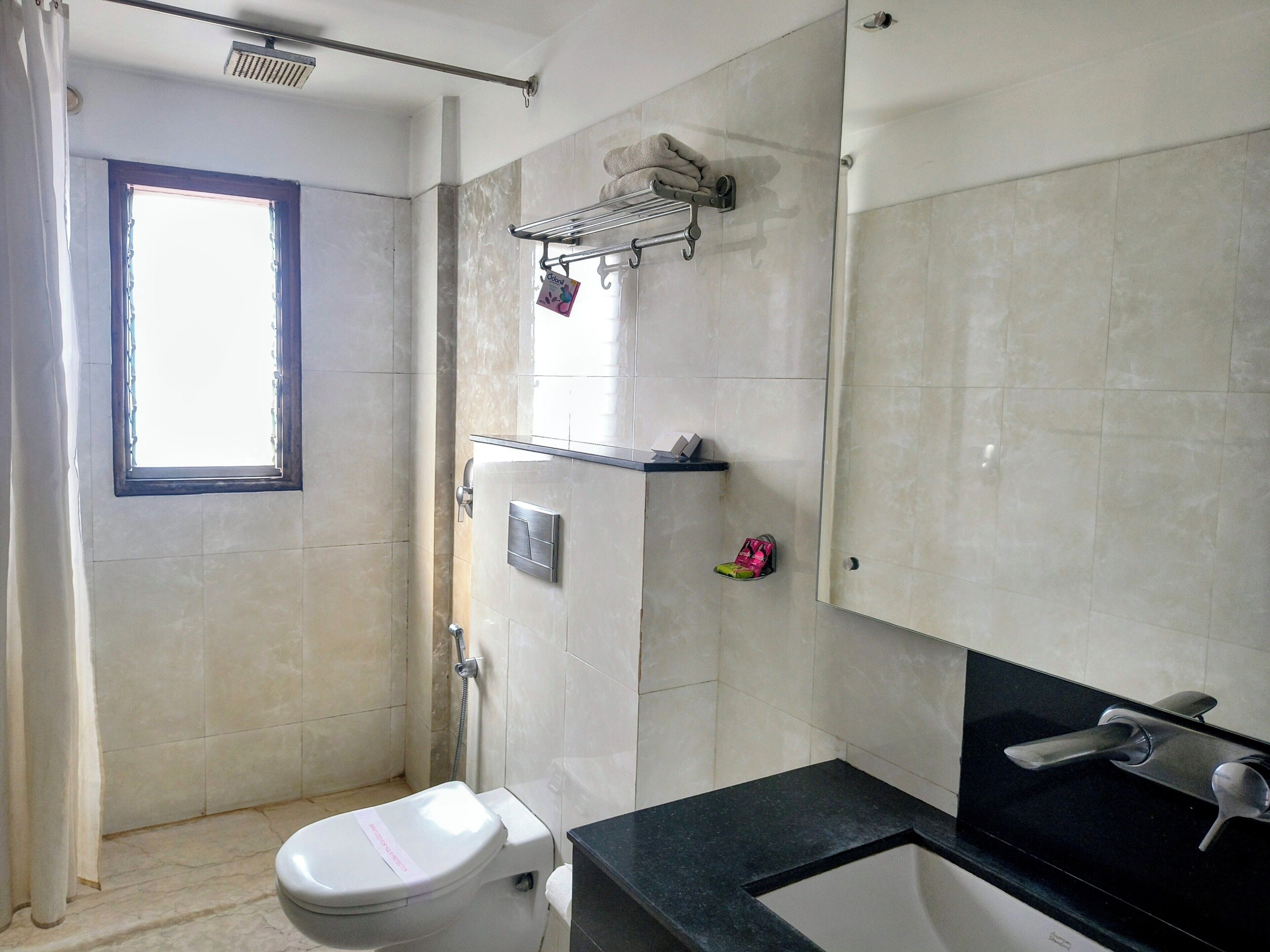Casa de banho com sanita, chuveiro, lavatório e suporte para toalhas.