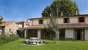 Um edifício com telhado ladrilhado, fachada de pedra e um jardim com mesa e cadeiras redondas.
