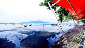 Uma praia com barcos, um toldo vermelho e montanhas ao fundo.