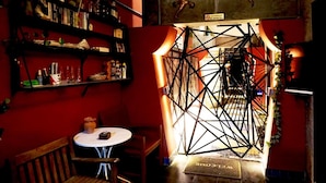 Uma área de bar com uma mesa redonda, prateleiras com garrafas e um portão de metal decorativo.