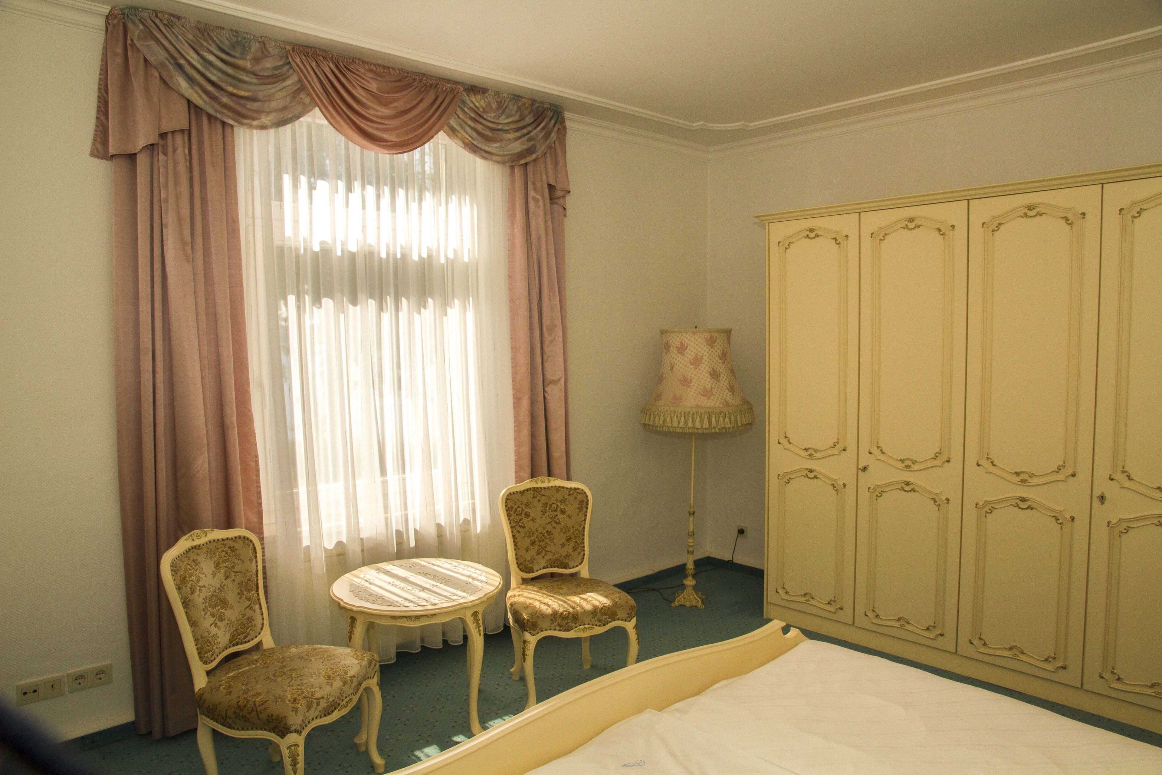 Quarto com cama, duas cadeiras, uma mesa, abajur e guarda-roupa.