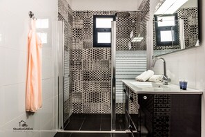 Uma casa de banho com azulejos estampados, chuveiro, lavatório com artigos de higiene e espelho.