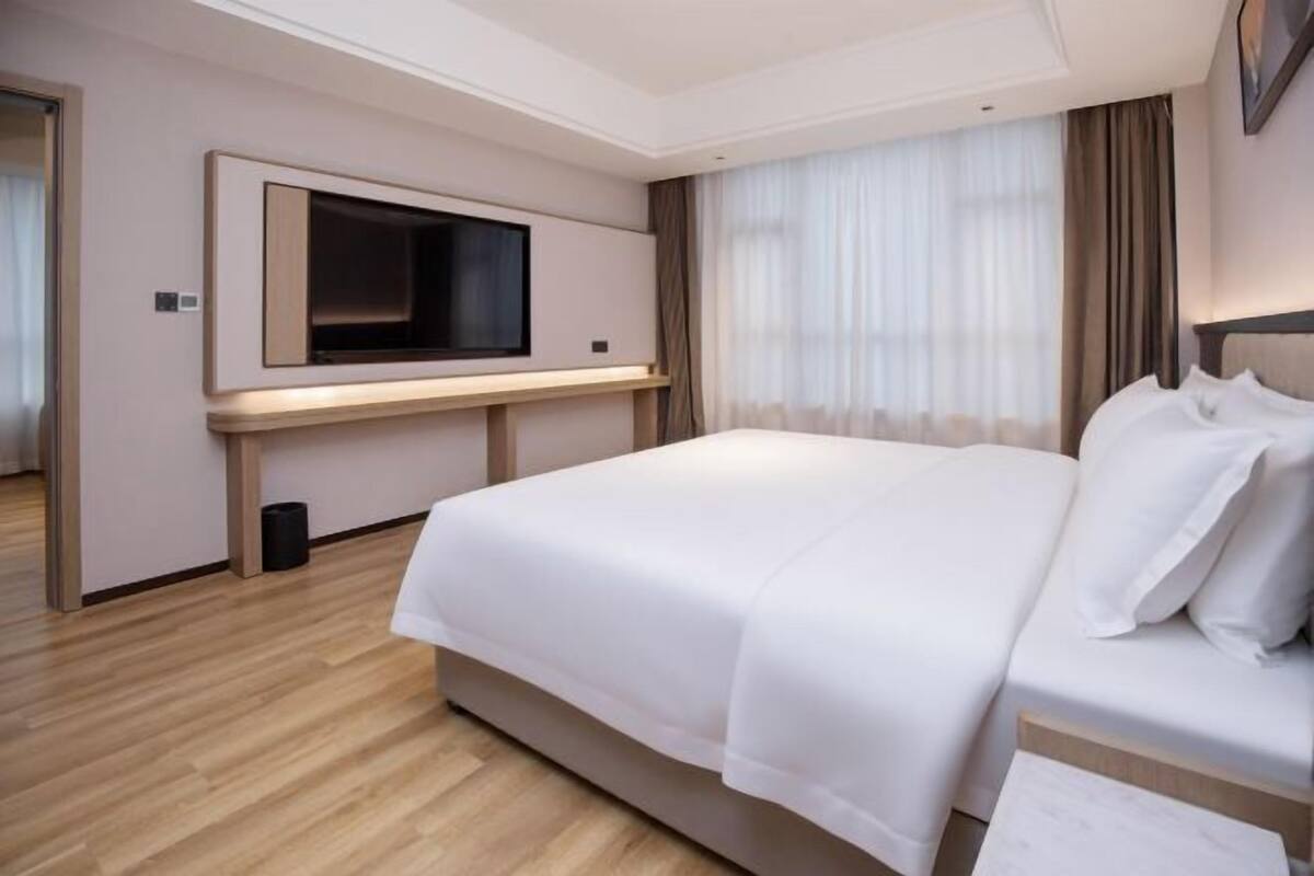 Quarto de hotel com uma cama grande, televisão fixada na parede e janela com cortinas.