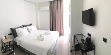 Quarto de hotel com cama, escrivaninha, cadeira, televisão e ar condicionado.