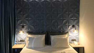 Quarto de hotel com cabeceira estofada, duas mesas de cabeceira com luminárias, cama com roupa de cama branca e um conjunto de toalhas sobre a cama.
