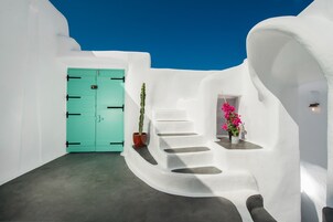 Interior com paredes brancas, uma porta turquesa, uma escada e plantas em vasos.