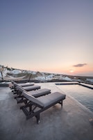 Uma área de piscina no terraço com espreguiçadeiras e vista para edifícios brancos ao fundo.