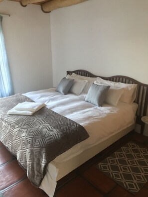 Uma cama bem arrumada com manta e almofadas estampadas, cabeceira de madeira e chão de azulejos.